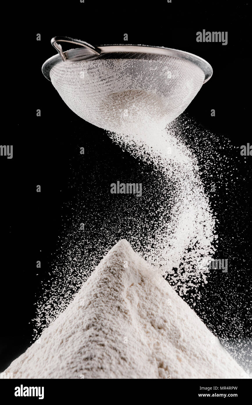 white flour falling from sieve on pile isolated on black Stock Photo - Alamy