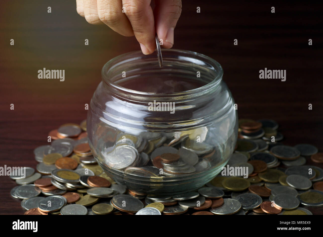 Hand putting money in jar hi-res stock photography and images - Alamy