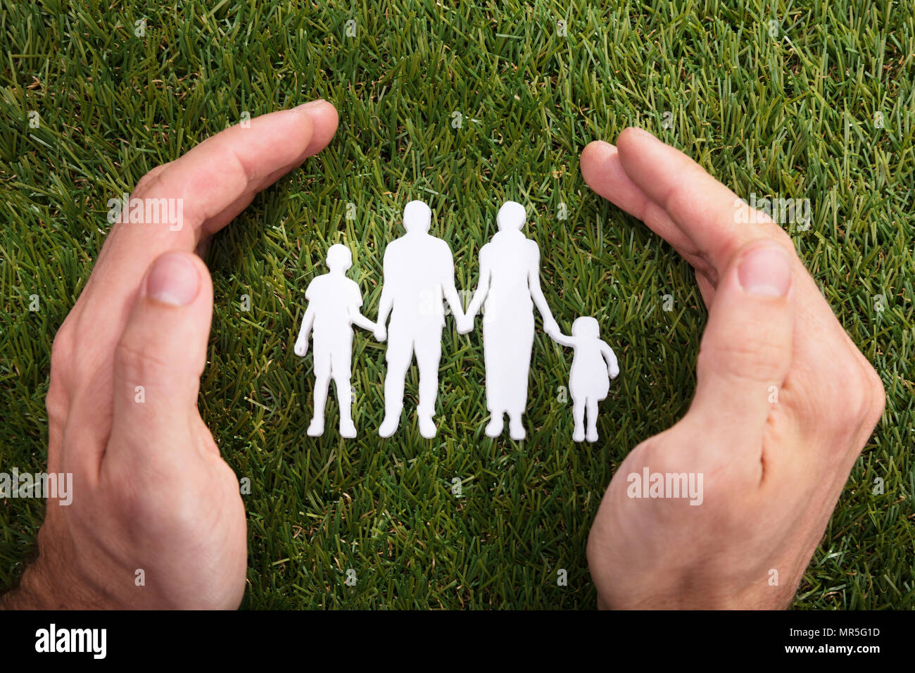 Elevated View Of A Human Hand Protecting Family Paper Cut Out On Green ...