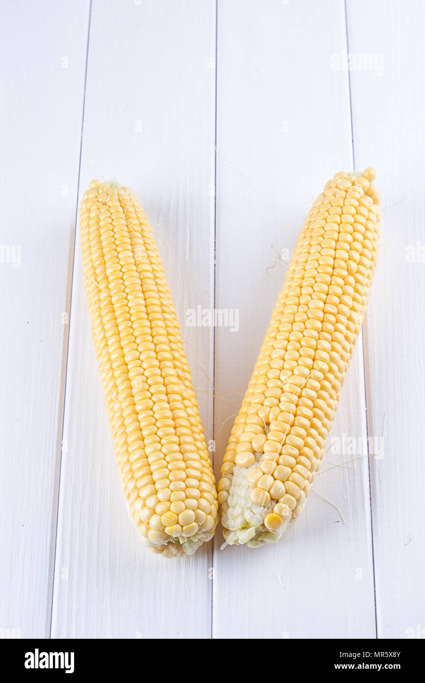 Two raw maize cobs at white wooden table background Stock Photo - Alamy