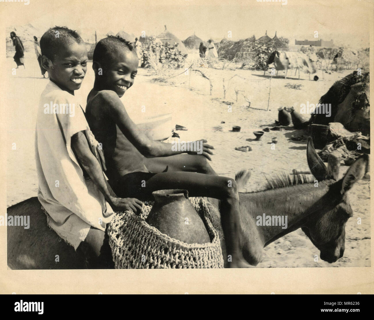 THERE ARE TWO KIDS RIDING A DONKEY WITH OTHER PEOPLE WALKING IN THE ...