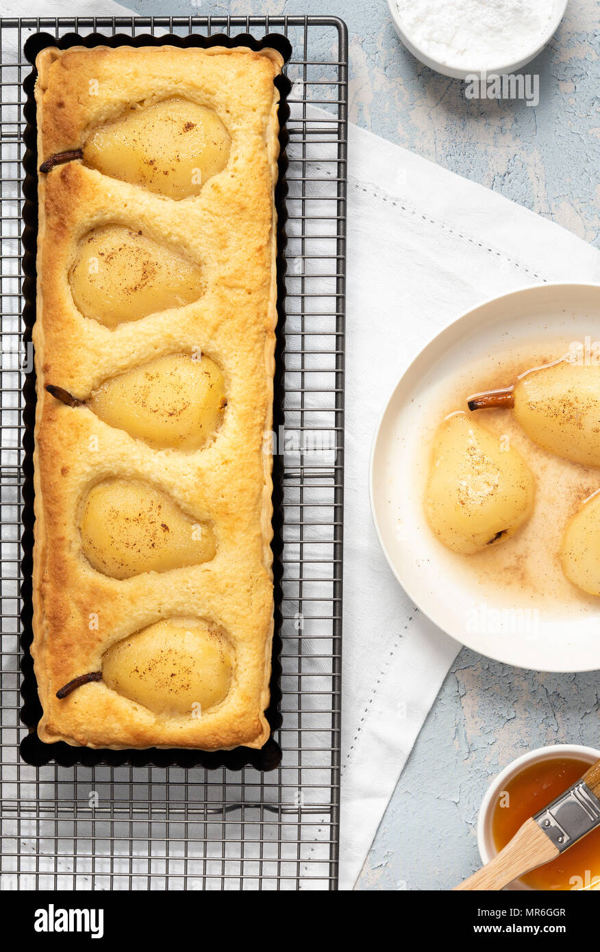 Baked Pear tart cooling on a wire rack with poached pears and a bowl of ...