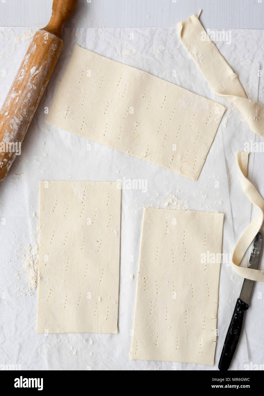 Three rectangular pieces of rolled pastry with a rolling pin and knife ...