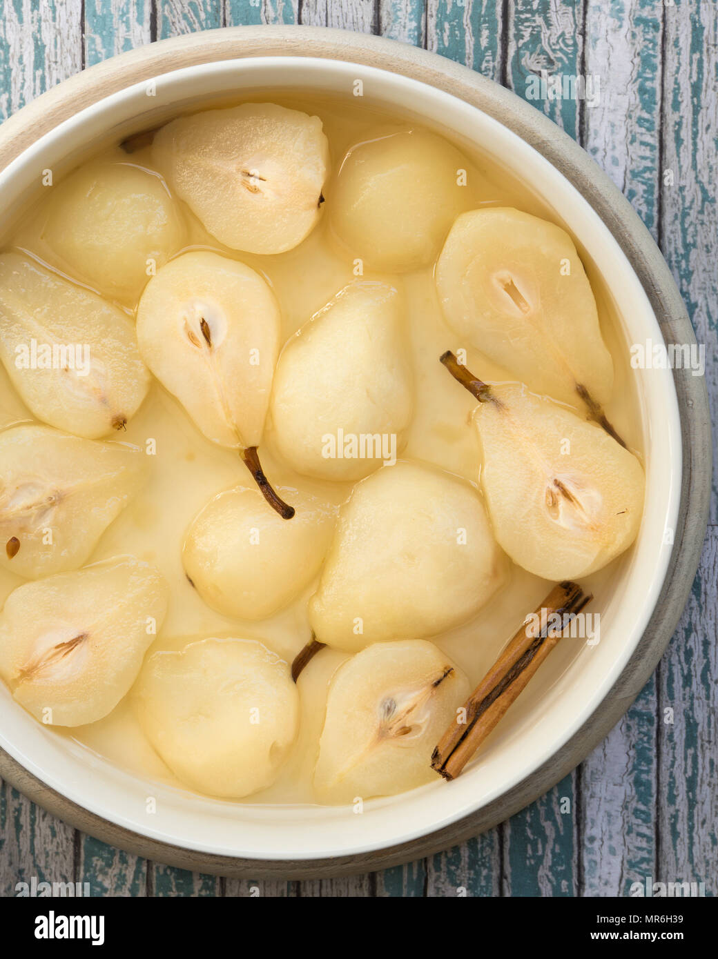 A bowl of poached pears and a cinnamon stick in light syrup on a blue ...