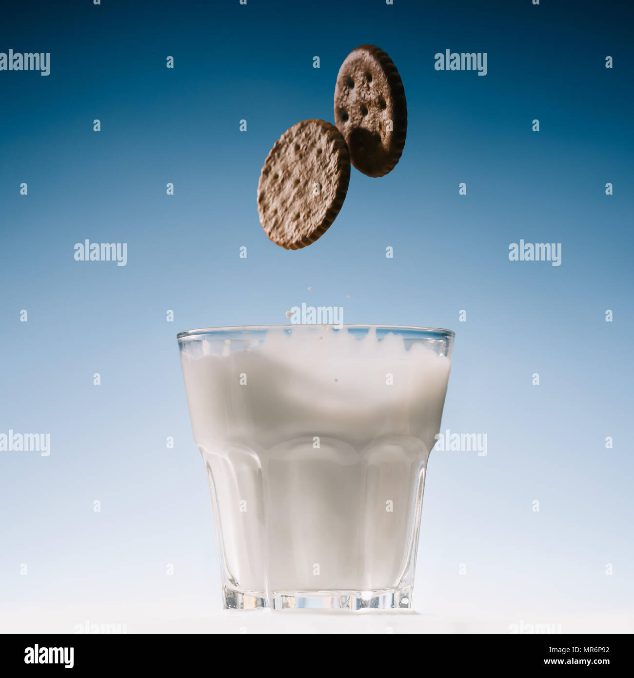 Two biscuits falling into glass of milk isolated on blue background ...