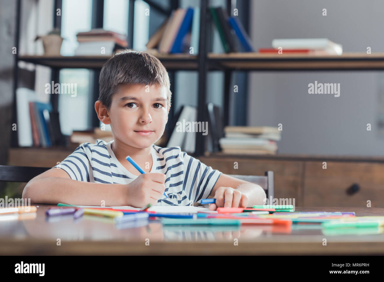portrait of boy drawing picture with colorful markers at table at home ...