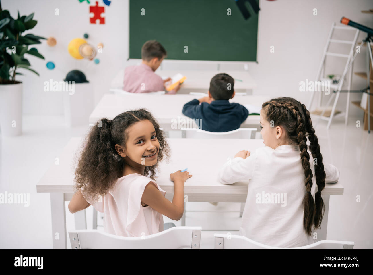 Back view of cute multiethnic kids sitting at school desks and studing ...