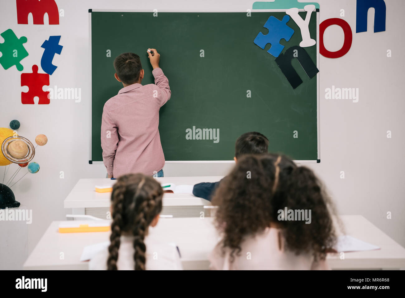 Back view of classmates looking at schoolboy answering near blank ...
