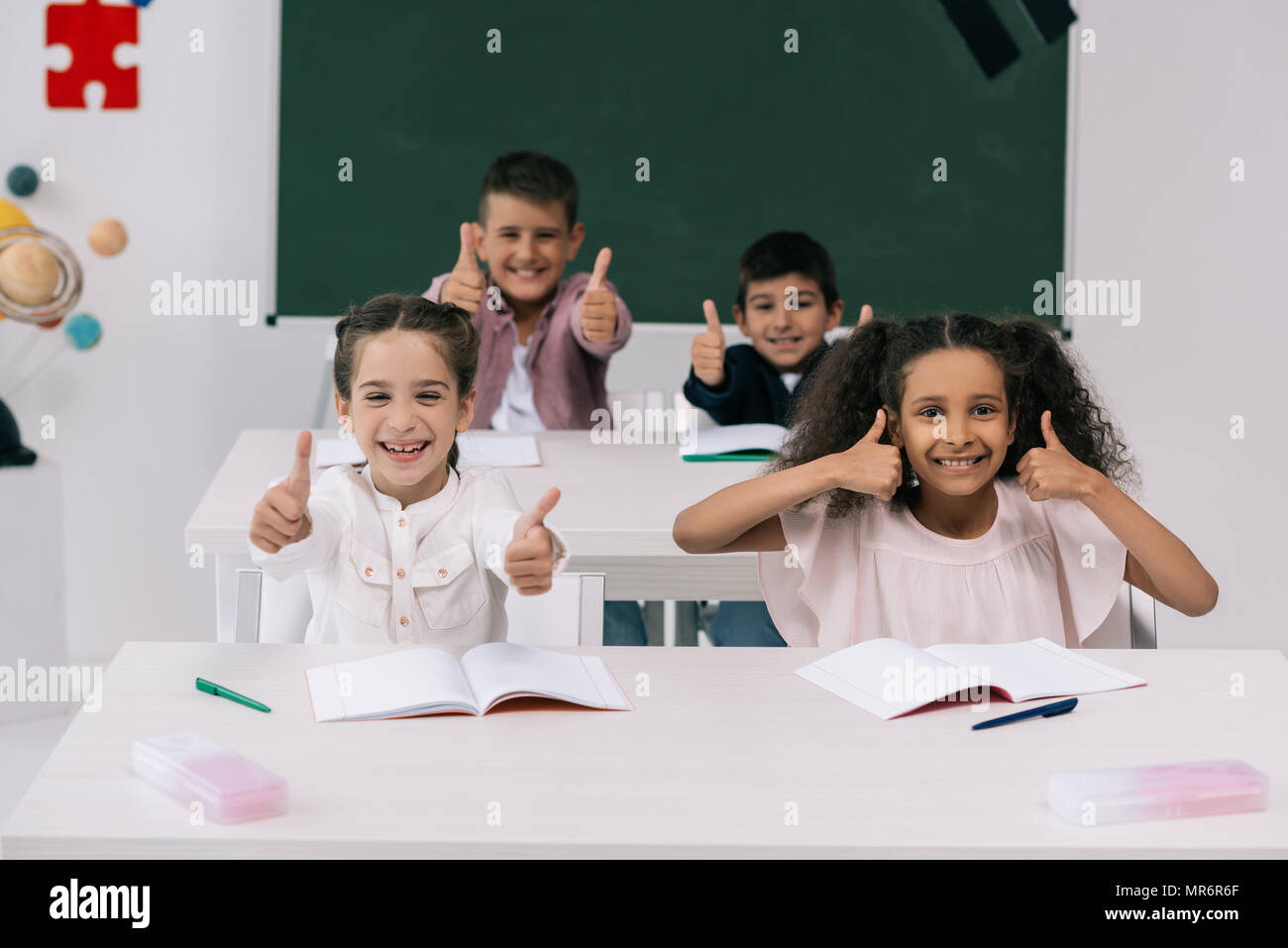 Cheerful multiethnic schoolkids showing thumbs up while sitting at ...