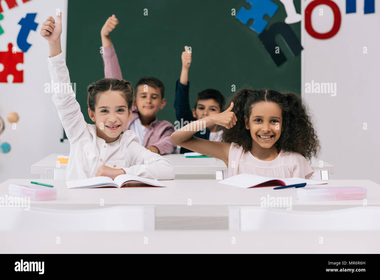 Cheerful multiethnic schoolkids showing thumbs up while sitting at ...