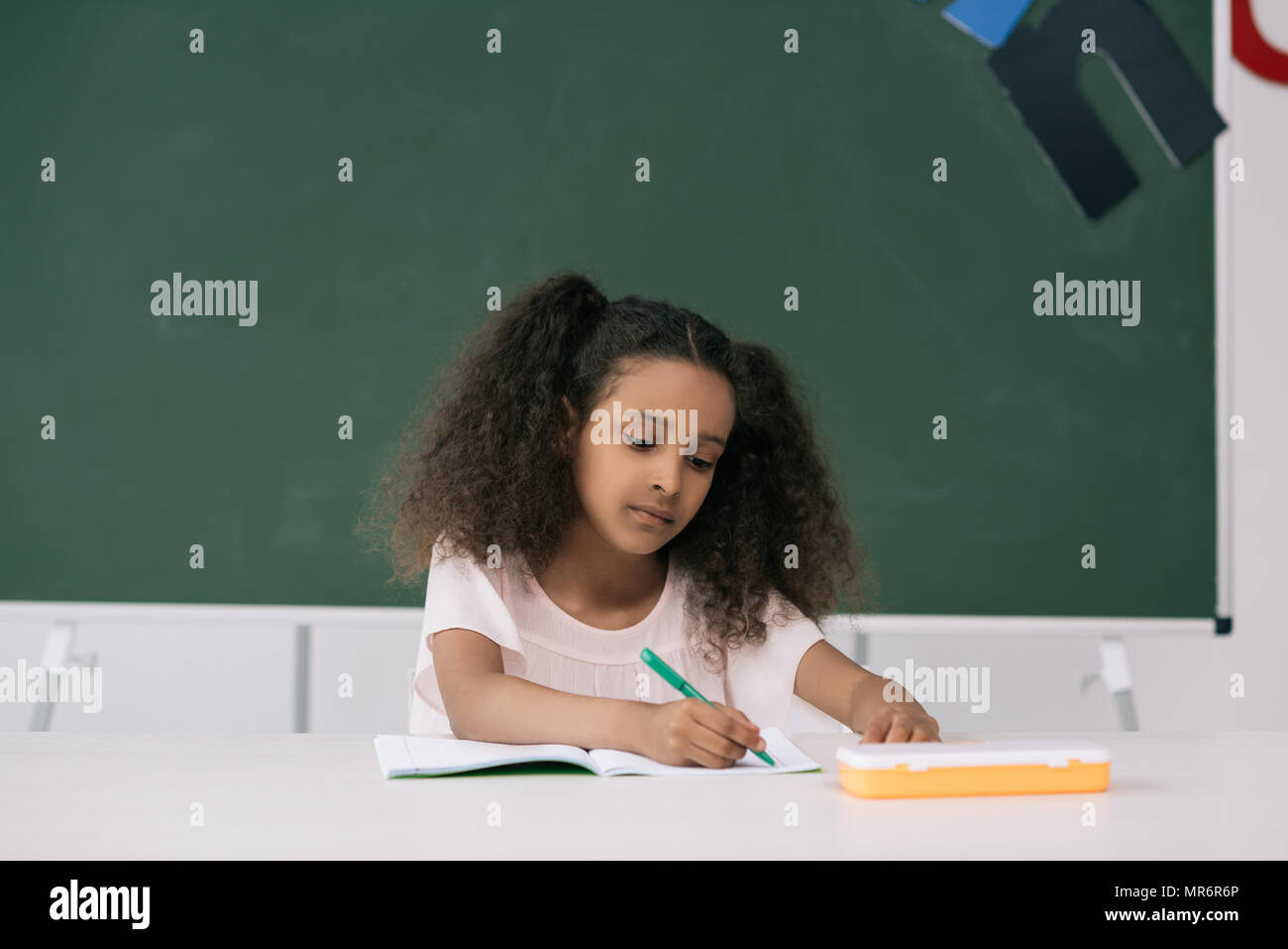Cute african american pupil writing in exercise book at lesson in class ...
