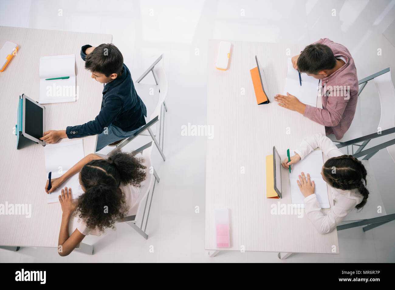 Overhead view of pupils using digital tablets while sitting at desks in ...