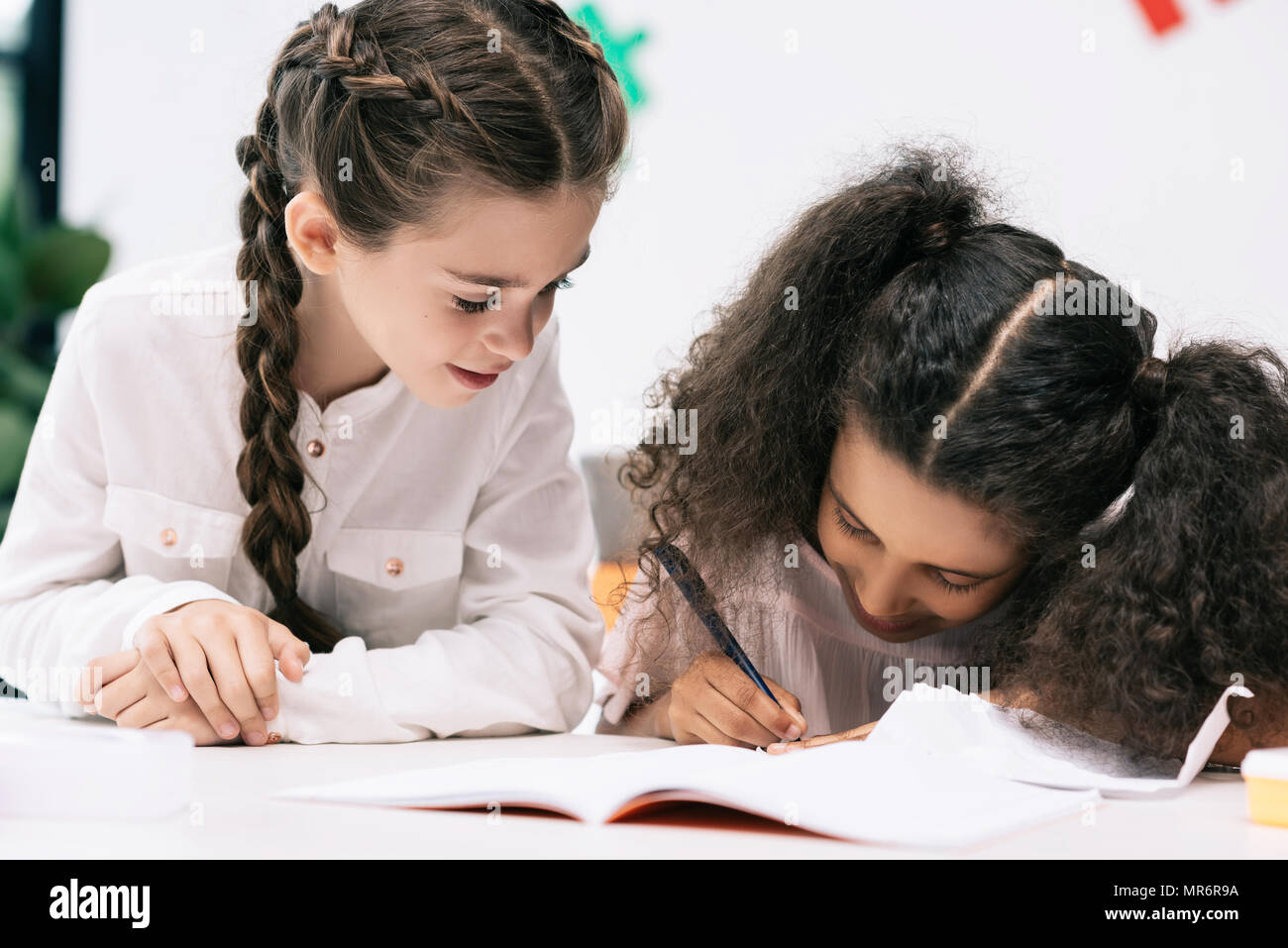 Cute smiling multiethnic schoolgirls studying together in classroom ...