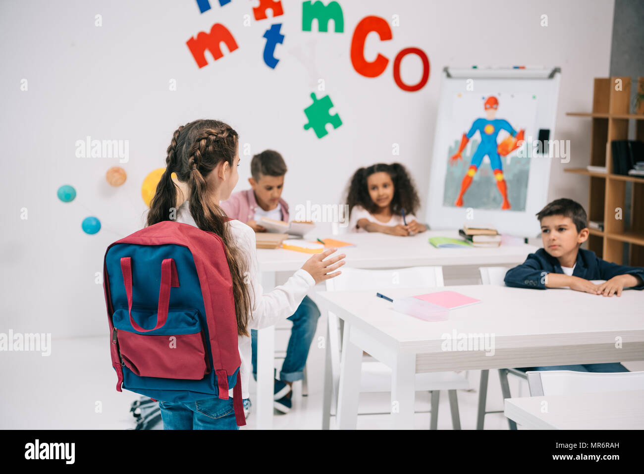 Back view of new pupil with backpack looking at classmates sitting at ...