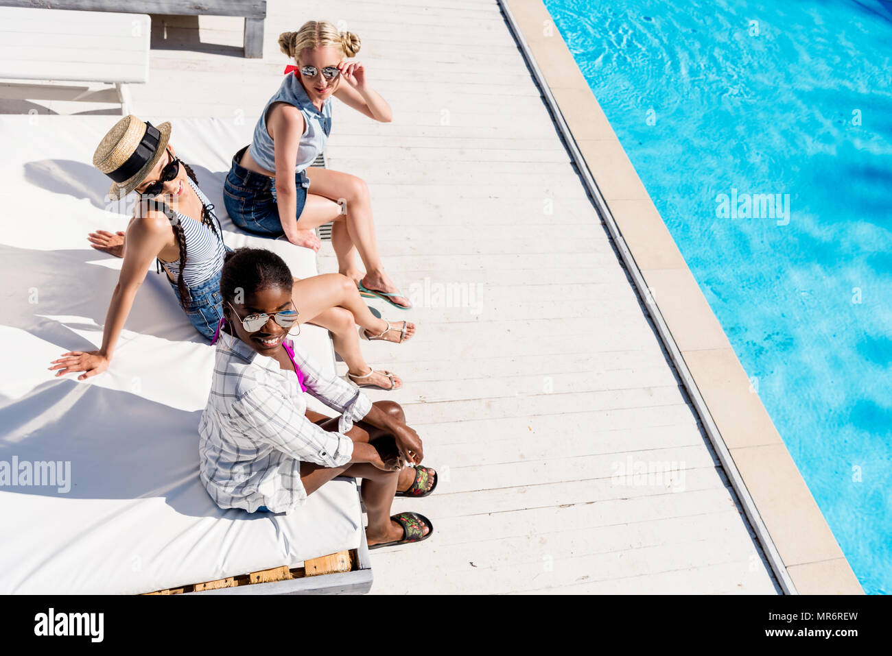 Young beautiful multiethnic women sitting at poolside at resort Stock ...