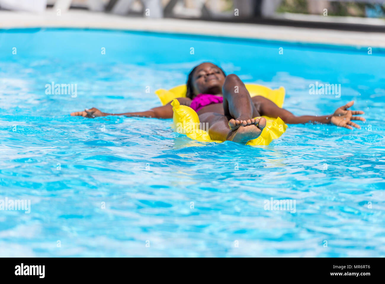 African american woman floating on inflatable mattress in swimming pool ...