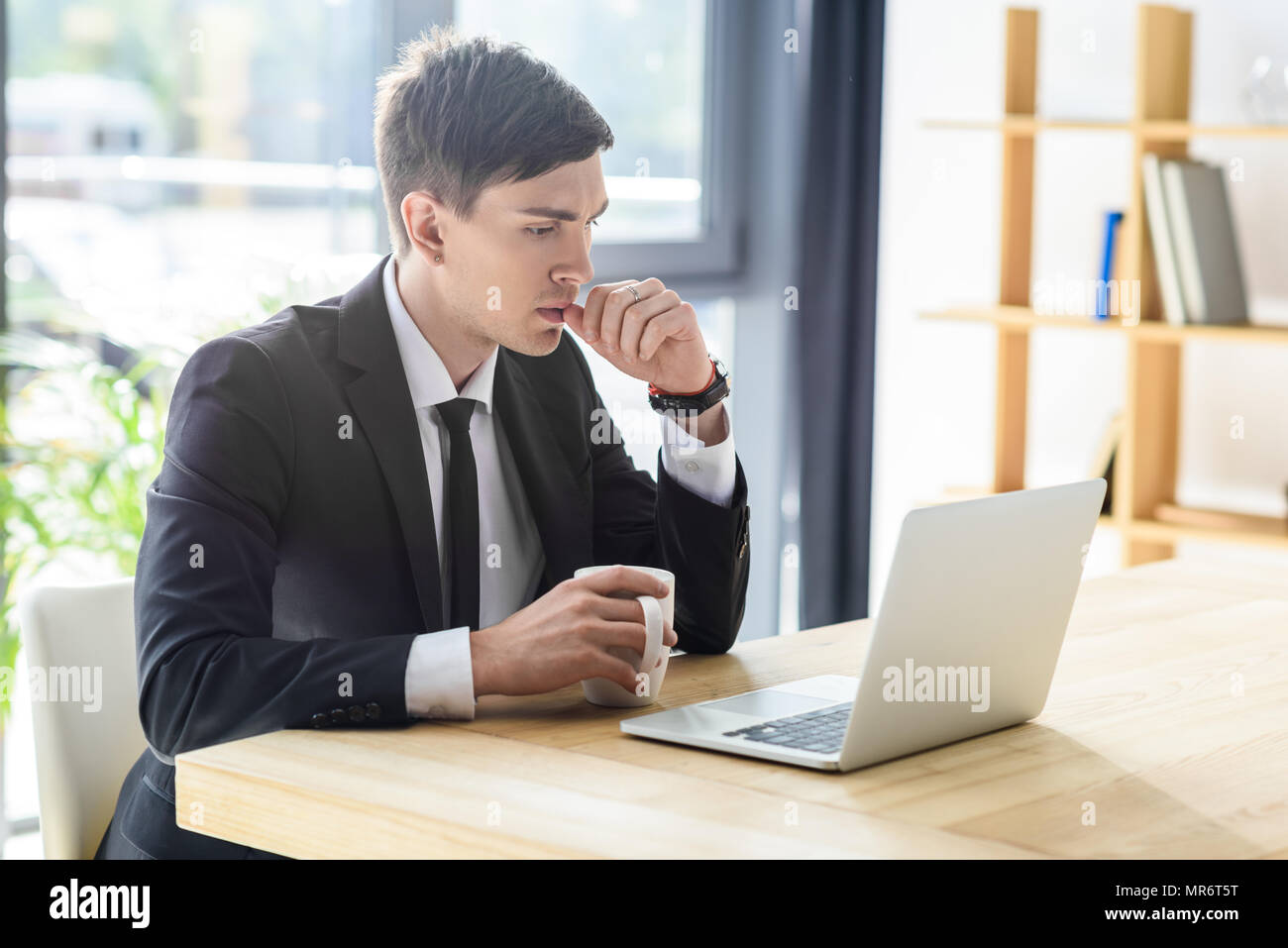Young businessman looking at laptop screen in modern office Stock Photo ...