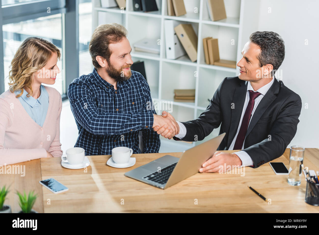 portrait of smiling lawyer and client shaking hands at meeting in ...
