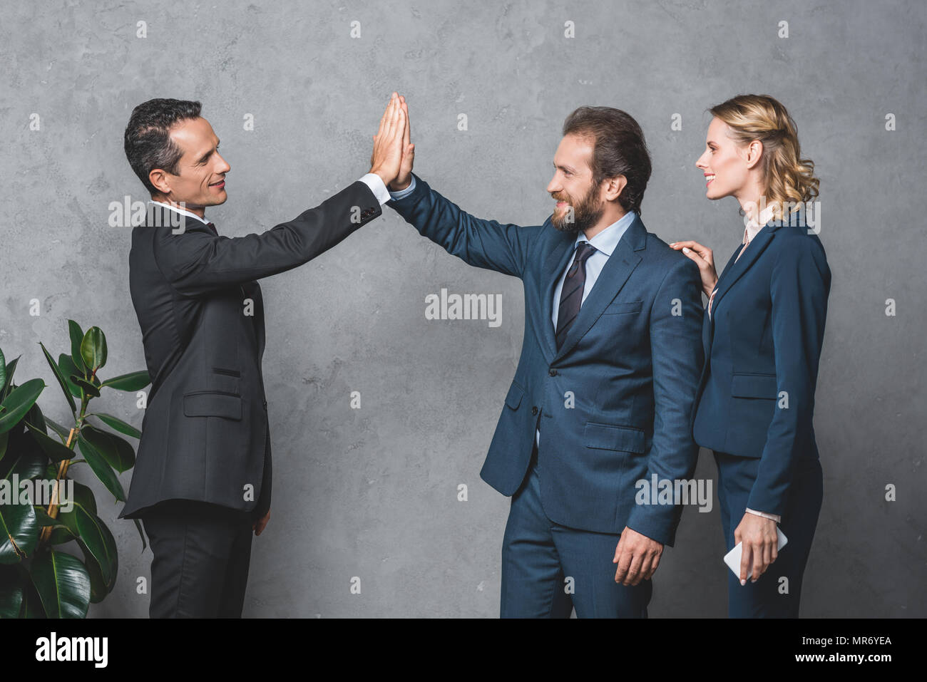 side view of smiling businesspeople giving high five to each other with ...