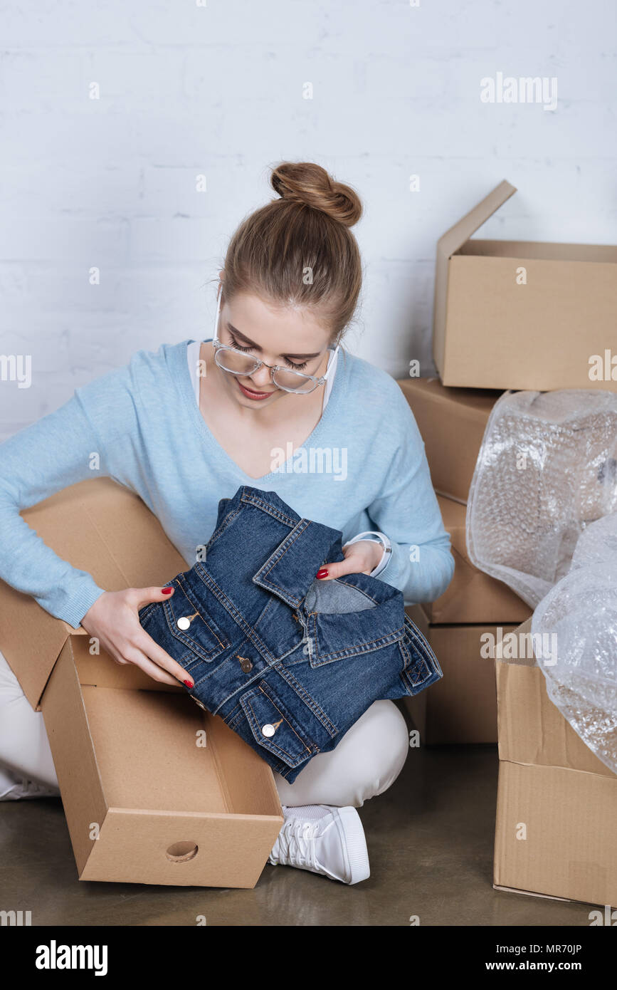 young entrepreneur putting denim jacket into cardboard box while ...