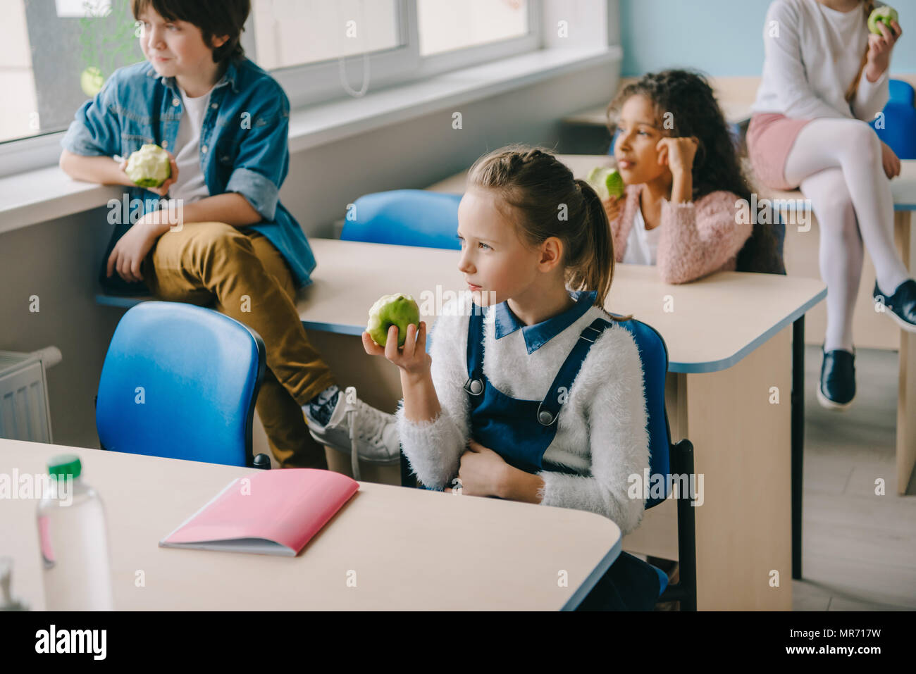 adorable schoolchildren eating apples at classroom while having break ...