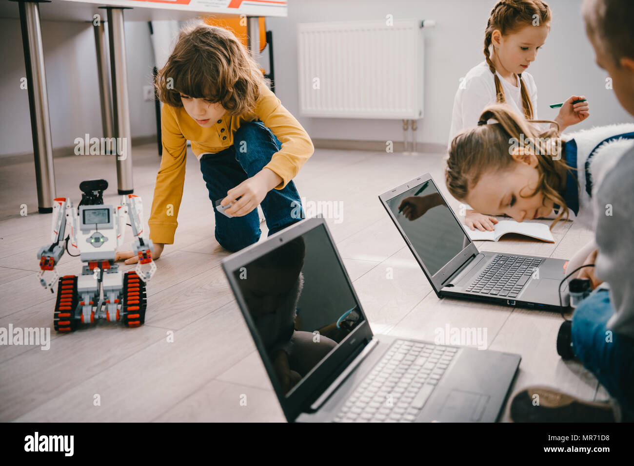 focused kids programming robots with computers while sitting on floor ...