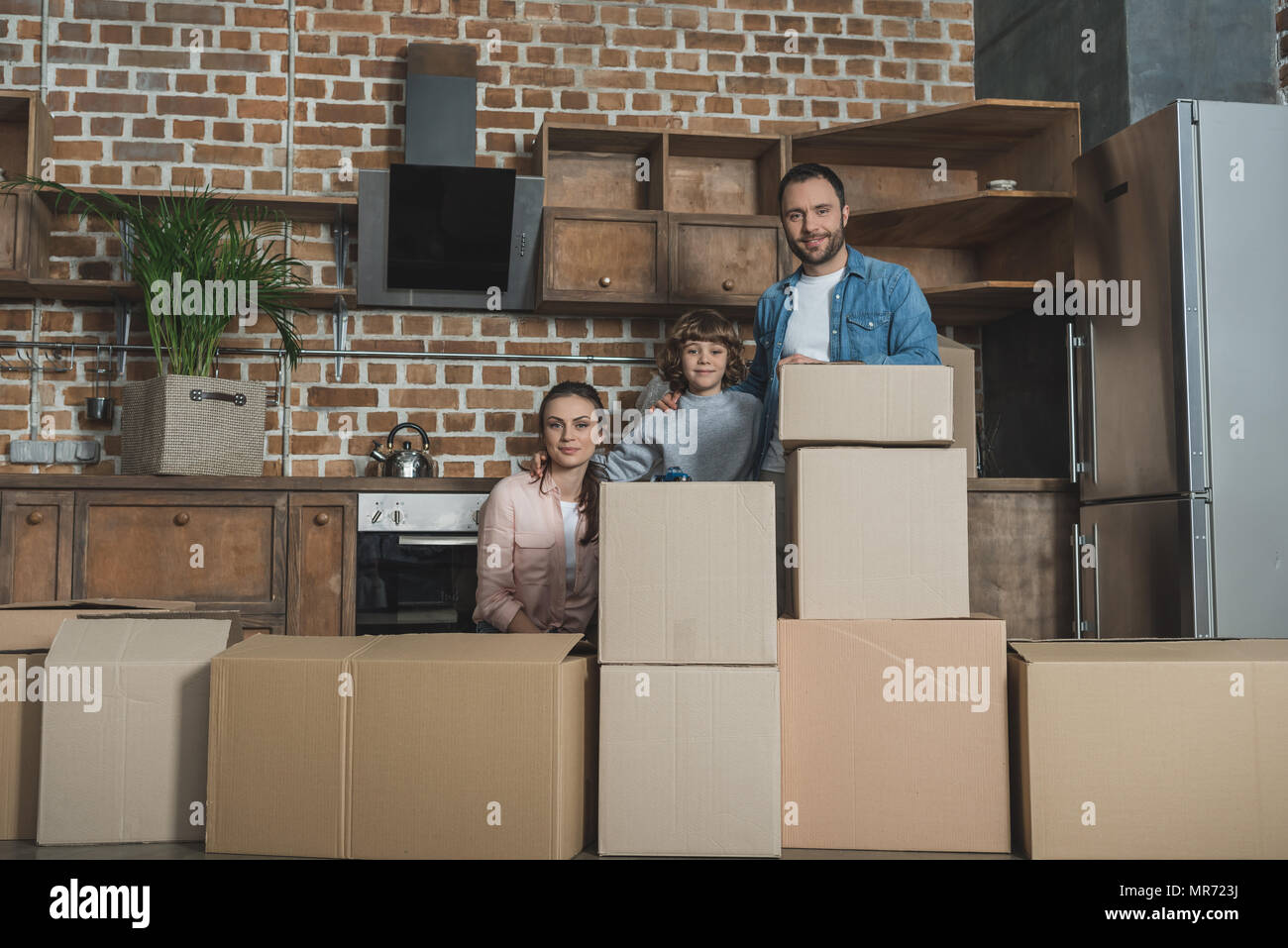 happy family with stacks of boxes smiling at camera while moving home ...