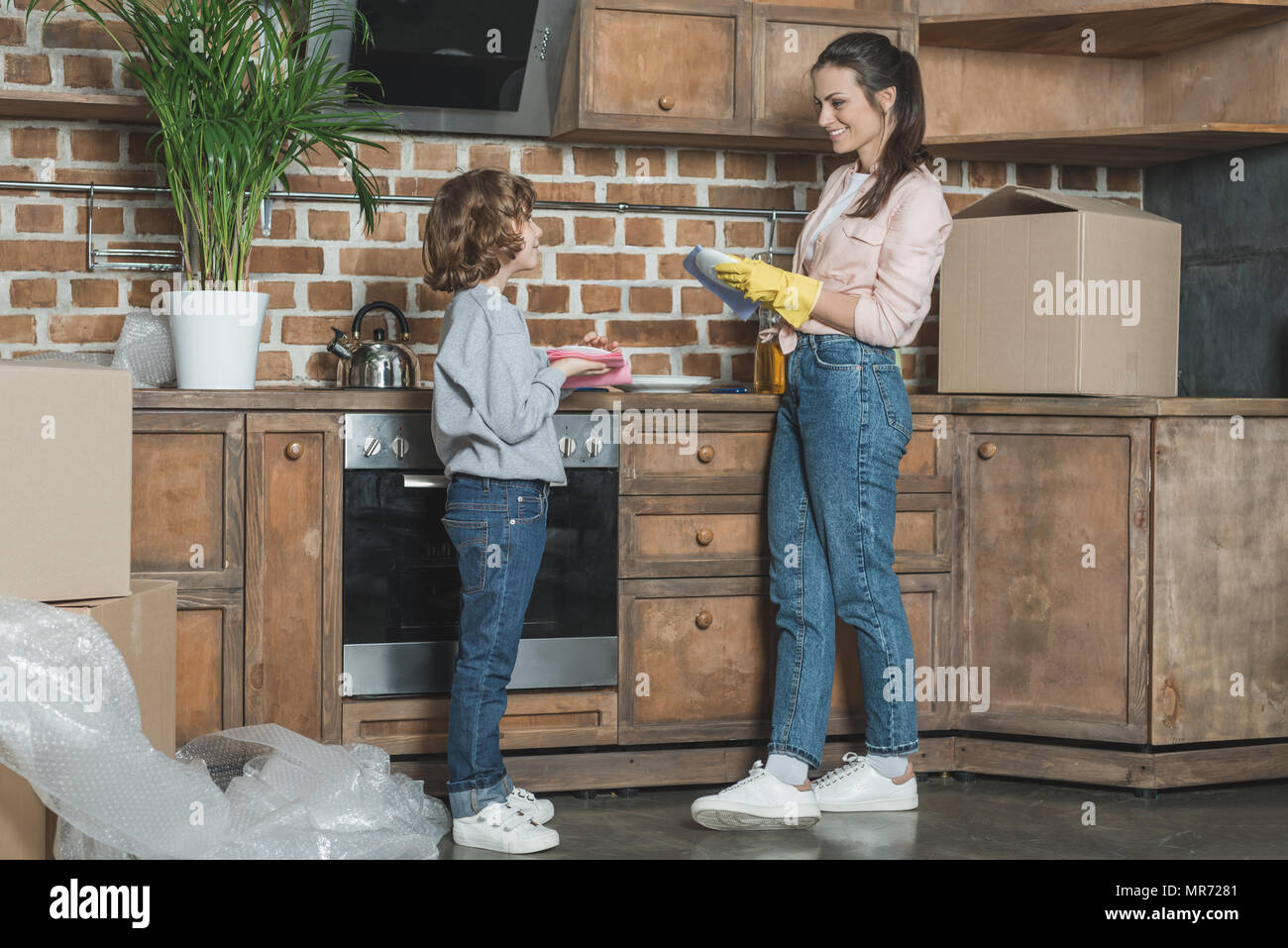 mother with son smiling each other while washing plates after ...
