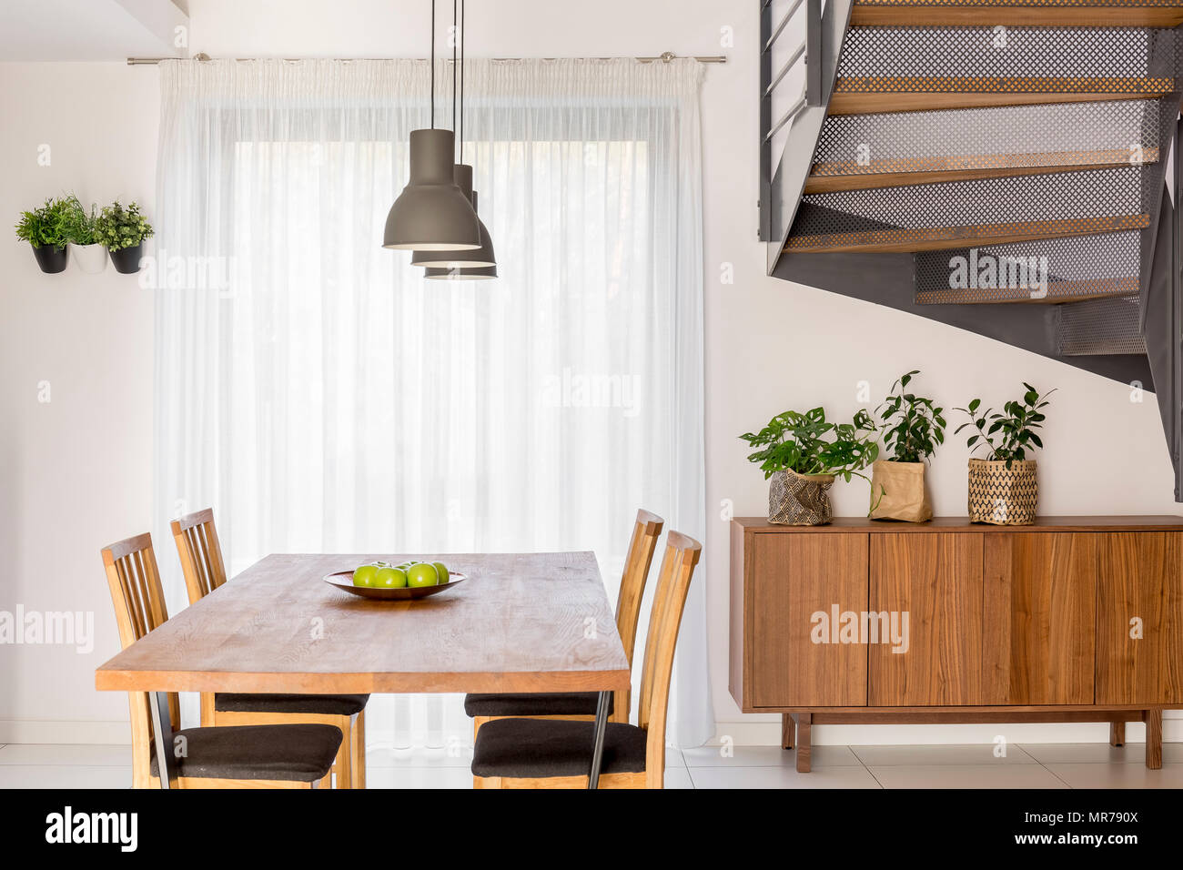 Dining room with communal table, lamp, dresser and stairs Stock Photo ...