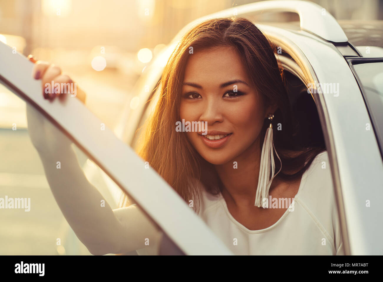 Young asian woman opening car door portrait on city background. Warm ...