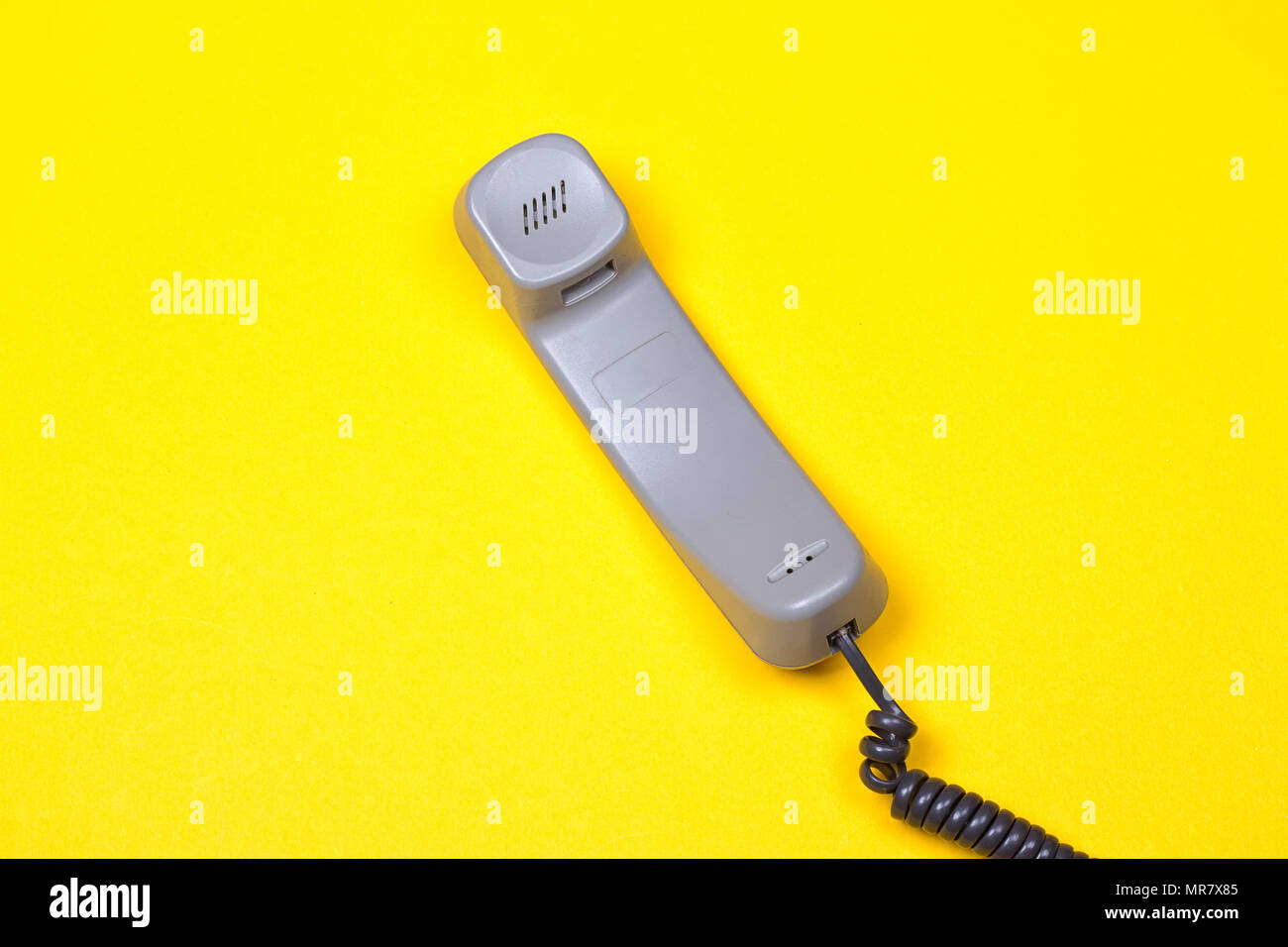Top view of gray telephone handset. receiver and cord on yellow ...