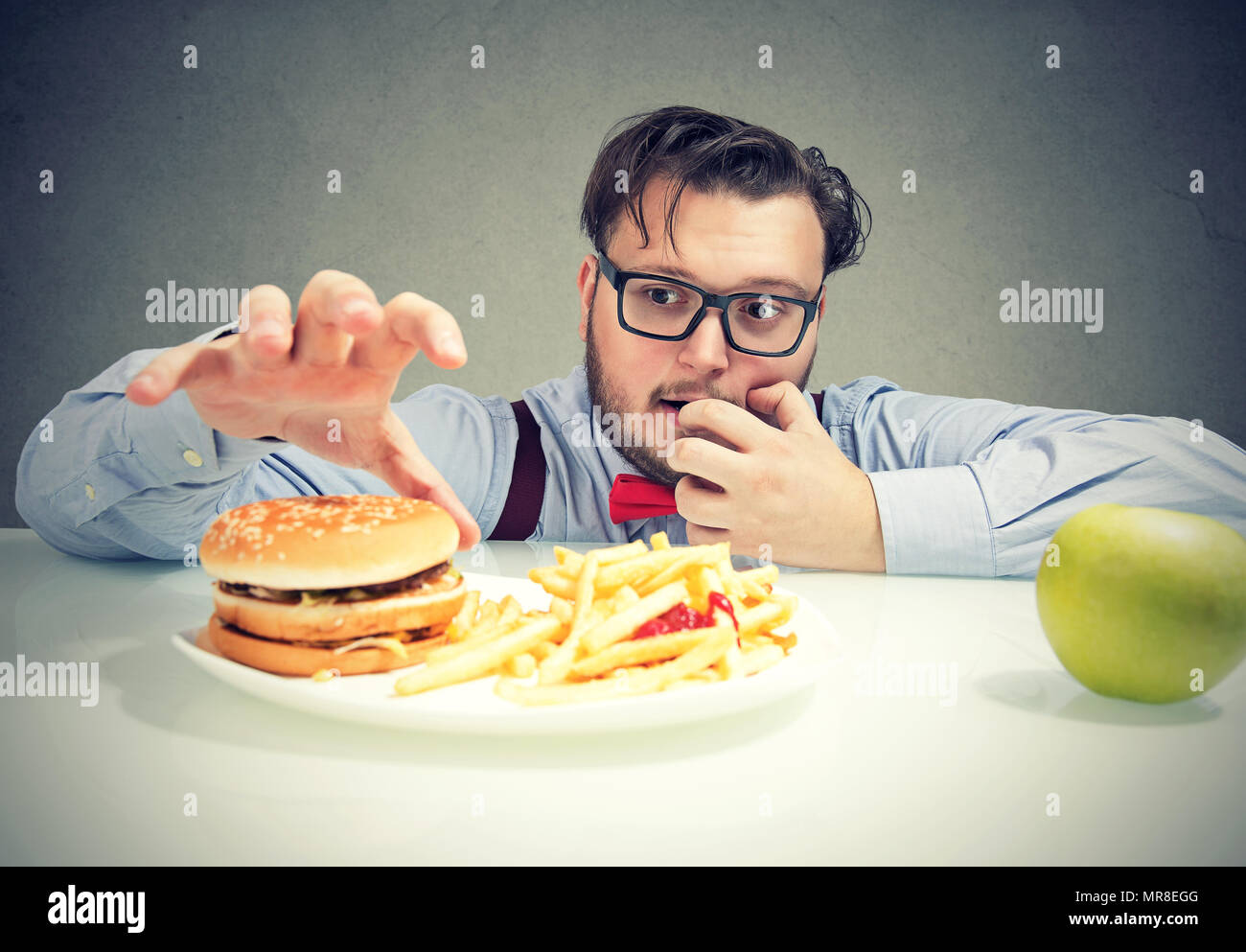 Young obese man in glasses having cravings for cheeseburger with fries ...