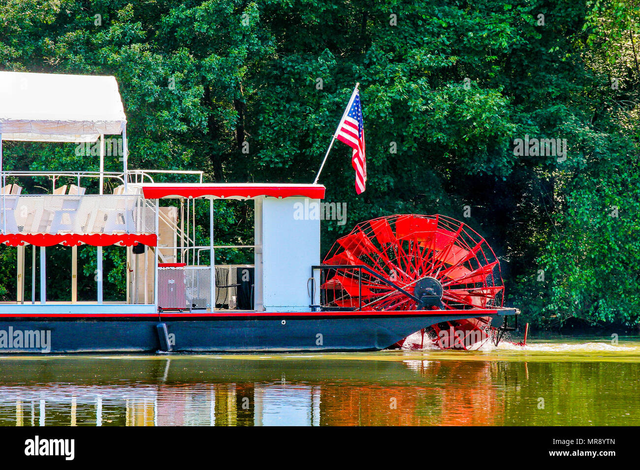 A red paddle wheel on a river boat with american flag on a calm river ...
