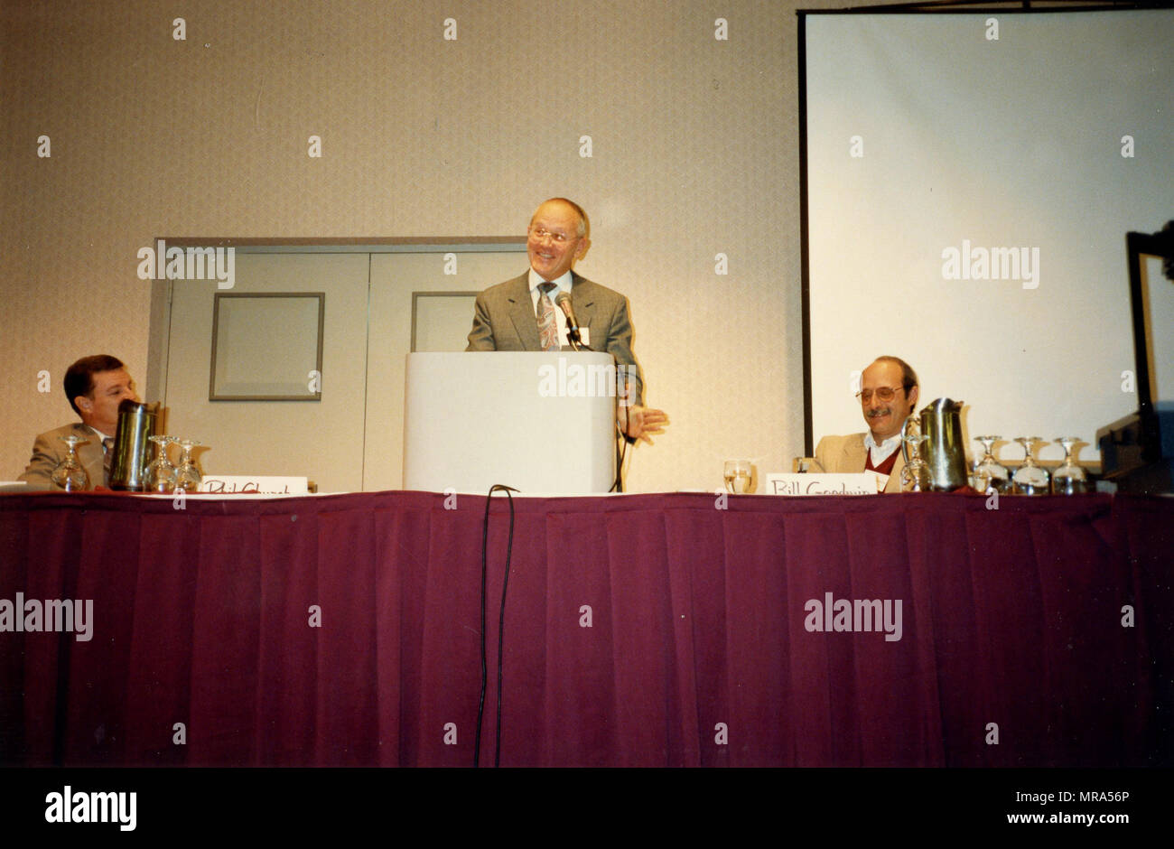 A MAN AT THE PODIUM WITH TWO OTHER MEN ON STAGE Stock Photo - Alamy