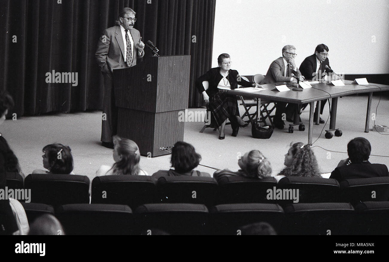 A MAN STANDING AT THE PODIUM GIVING A SPEECH WITH TWO OTHER PEOPLE ON ...
