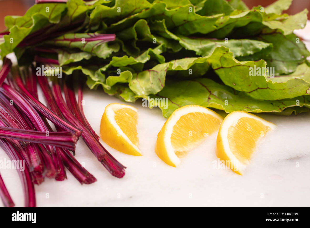 Fresh cut beet stems, leaves and lemon wedges on a marble cutting board ...