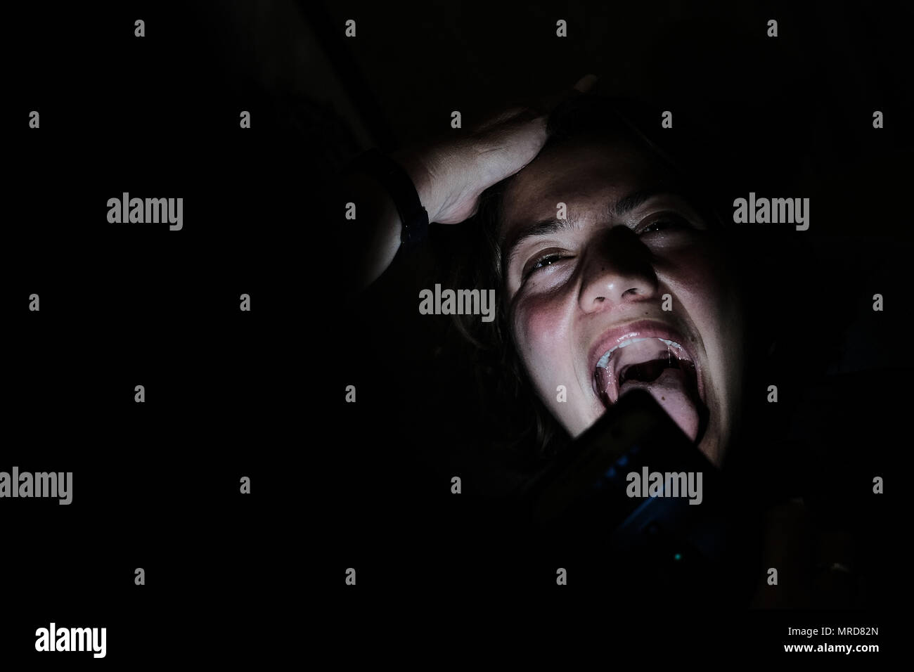Young woman with mouth wide open lit by cellphone flashlight in dark ...