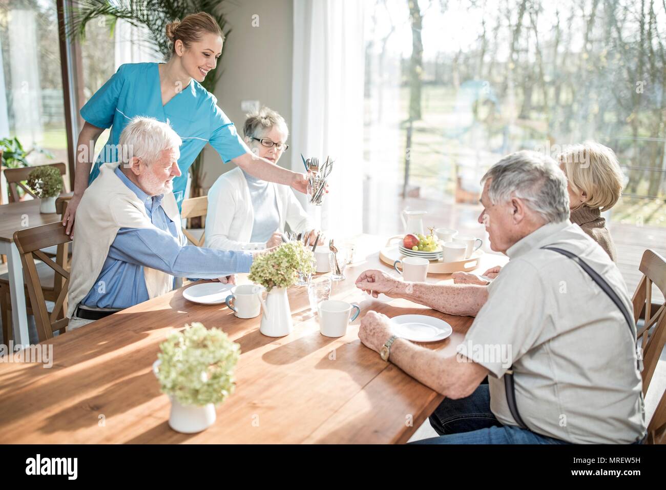Female care worker serving senior adults at dinner table in care home ...