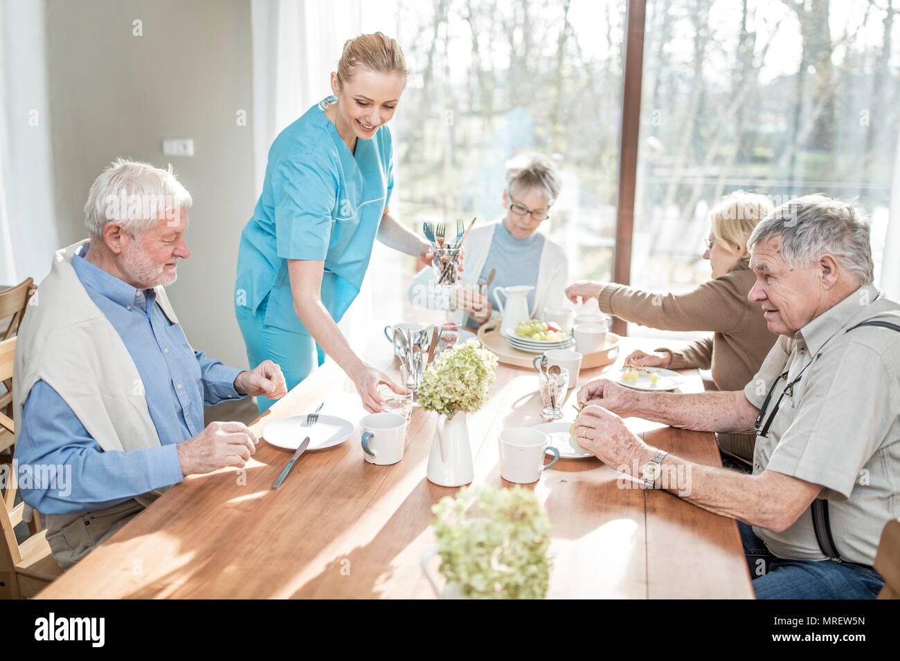 Female care worker serving senior adults at dinner table in care home ...