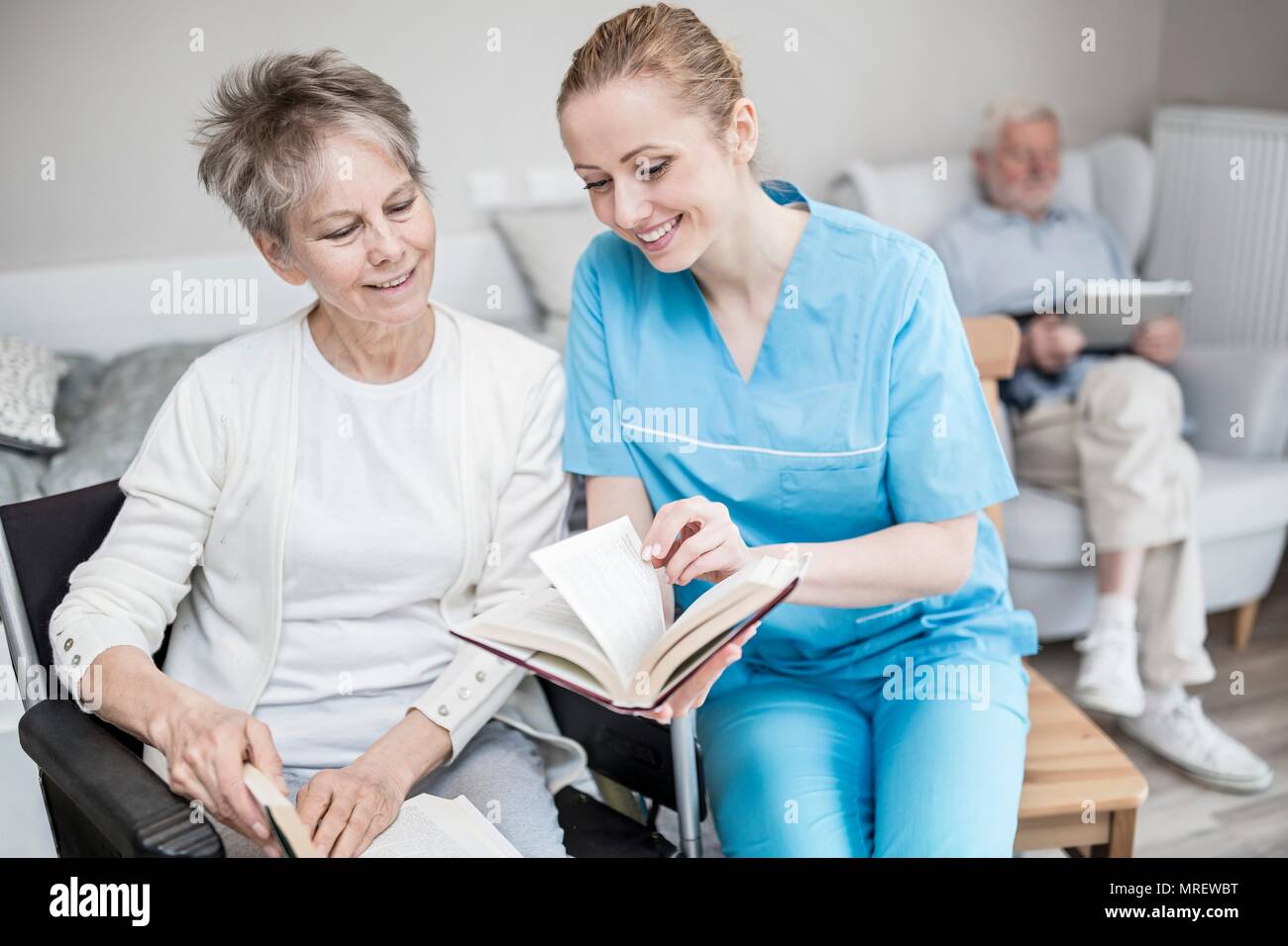 Care worker reading book with senior woman in care home Stock Photo - Alamy