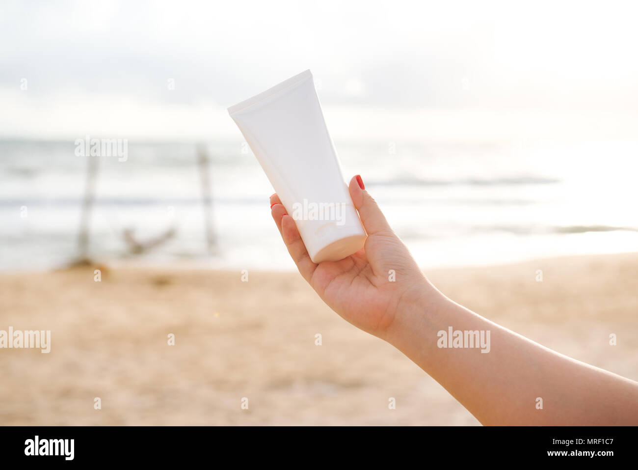 Woman hand holding sunscreen on the beach with the sea in blue sky ...