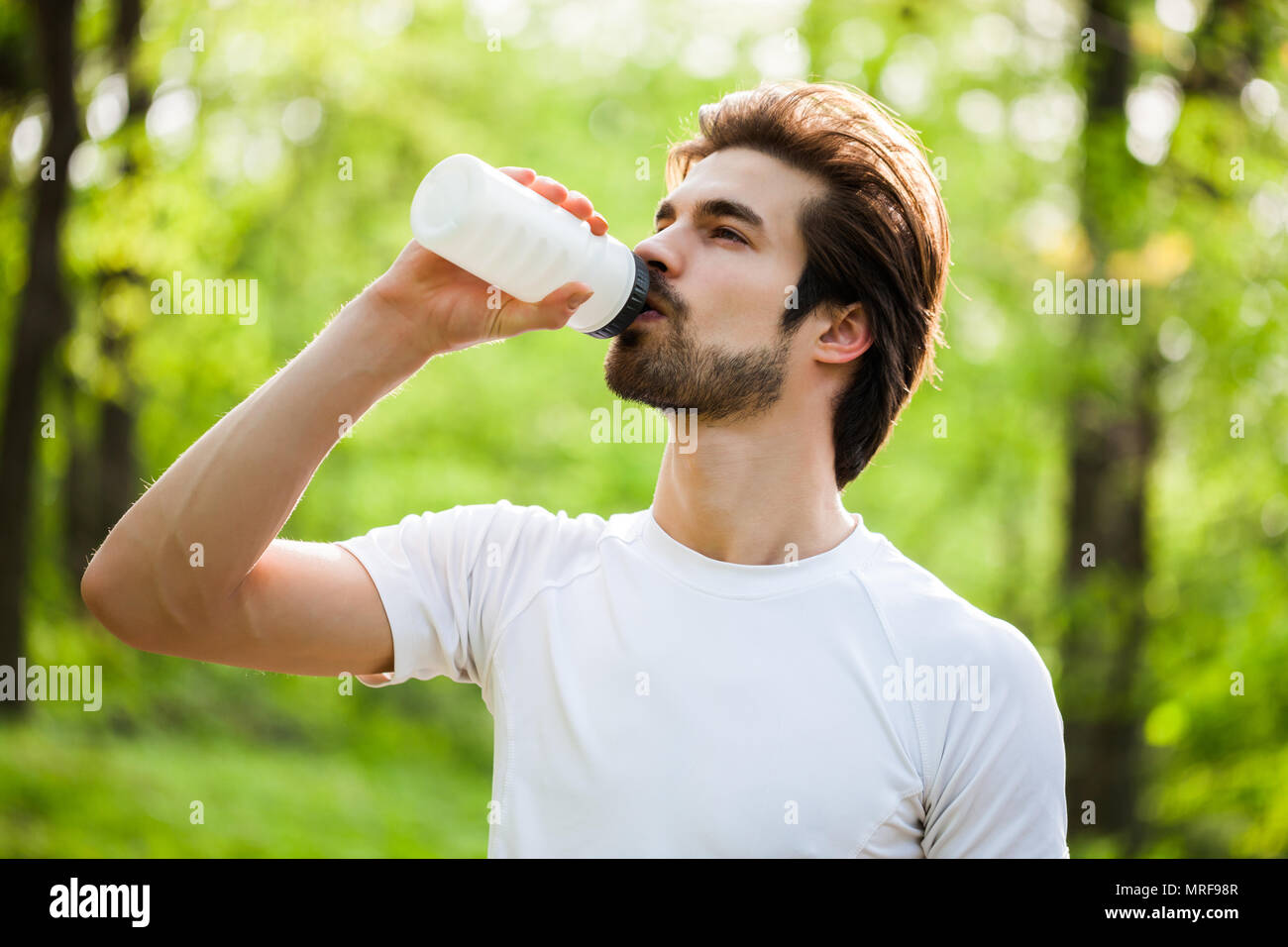 Young man is exercising in park. He is drinking water Stock Photo - Alamy