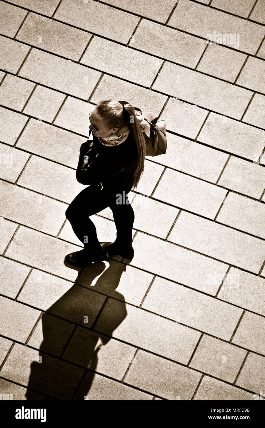 woman walking in the street a strong shadow projected on the pavement ...
