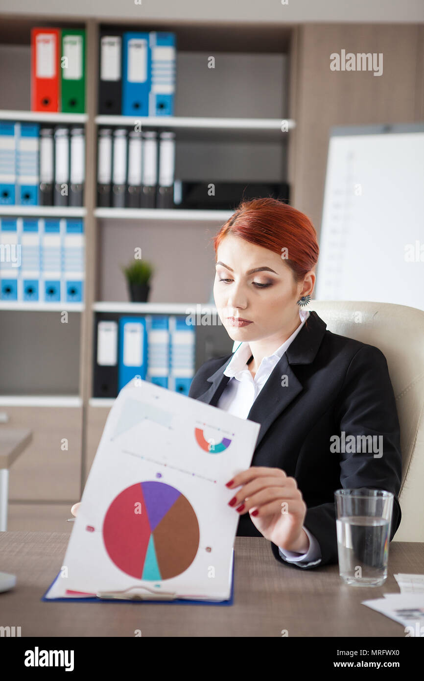 Businesswoman in her office checking documents with diagrams on them ...