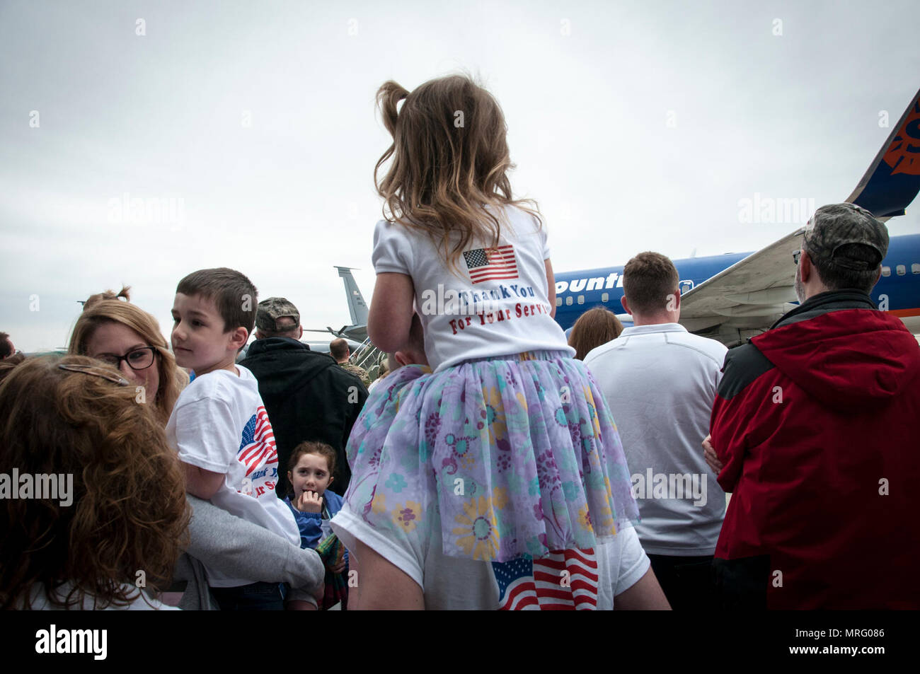 A little girl sits atop the shoulders of a family member as they wait ...