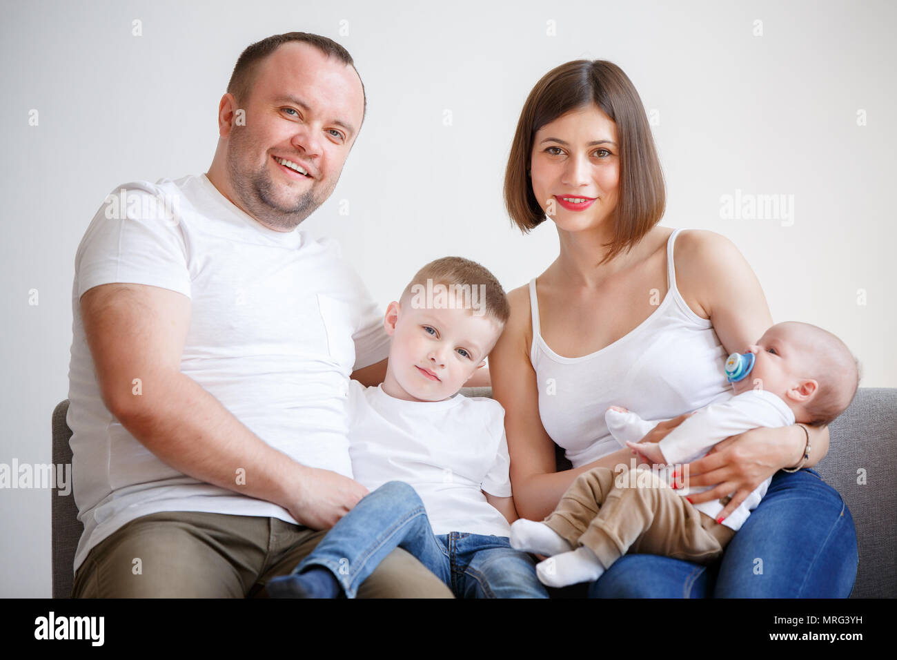 Picture of happy married couple with two young sons sitting on sofa ...