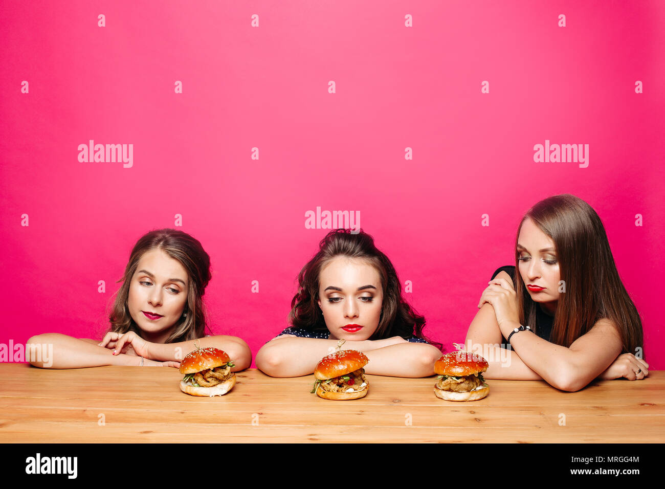 Three sad girls on diet looking at burgers on table Stock Photo - Alamy