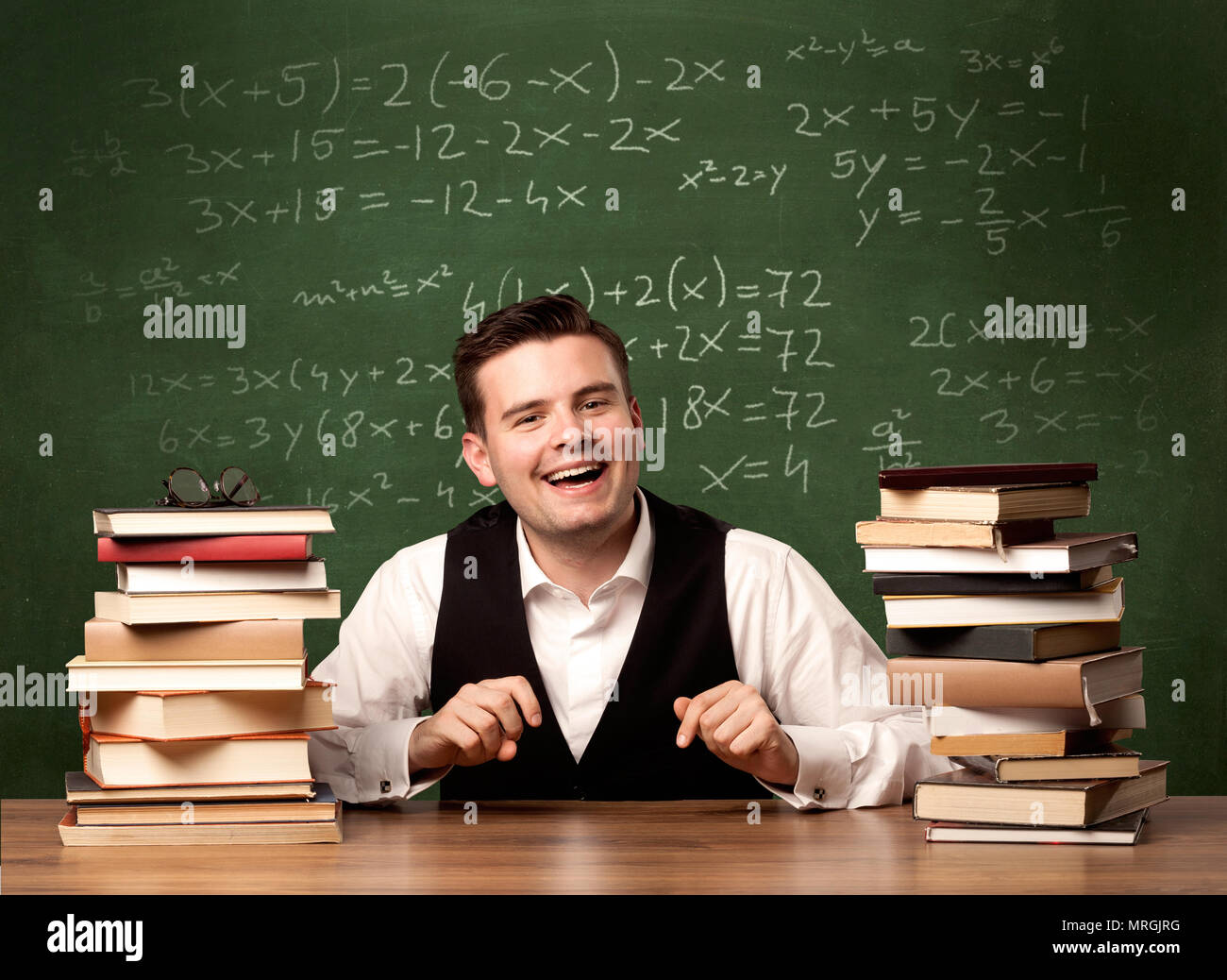 A young ambitious teacher in glasses sitting at classroom desk with ...