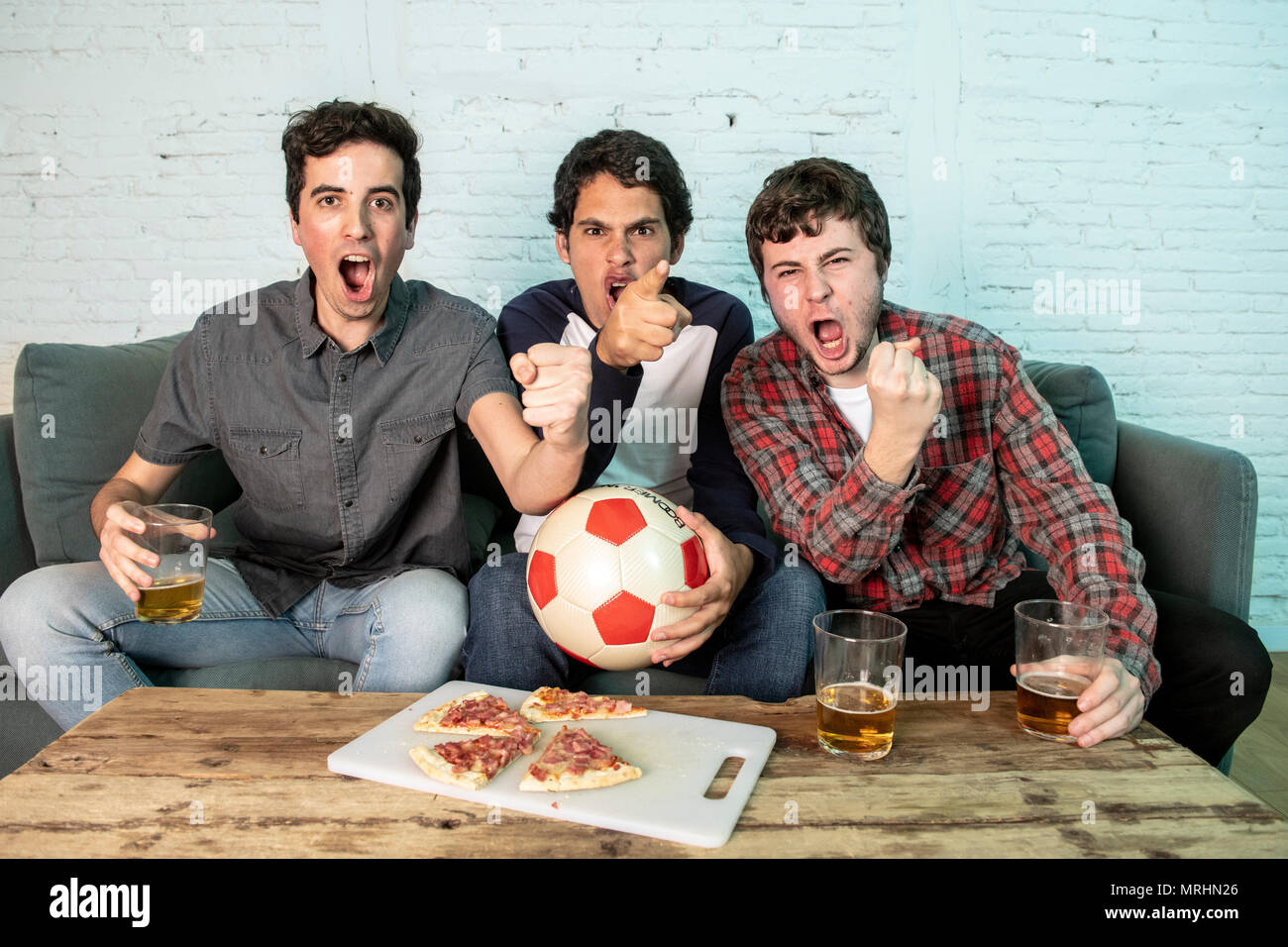 a happy and excited young group of football fans sitting on the sofa ...