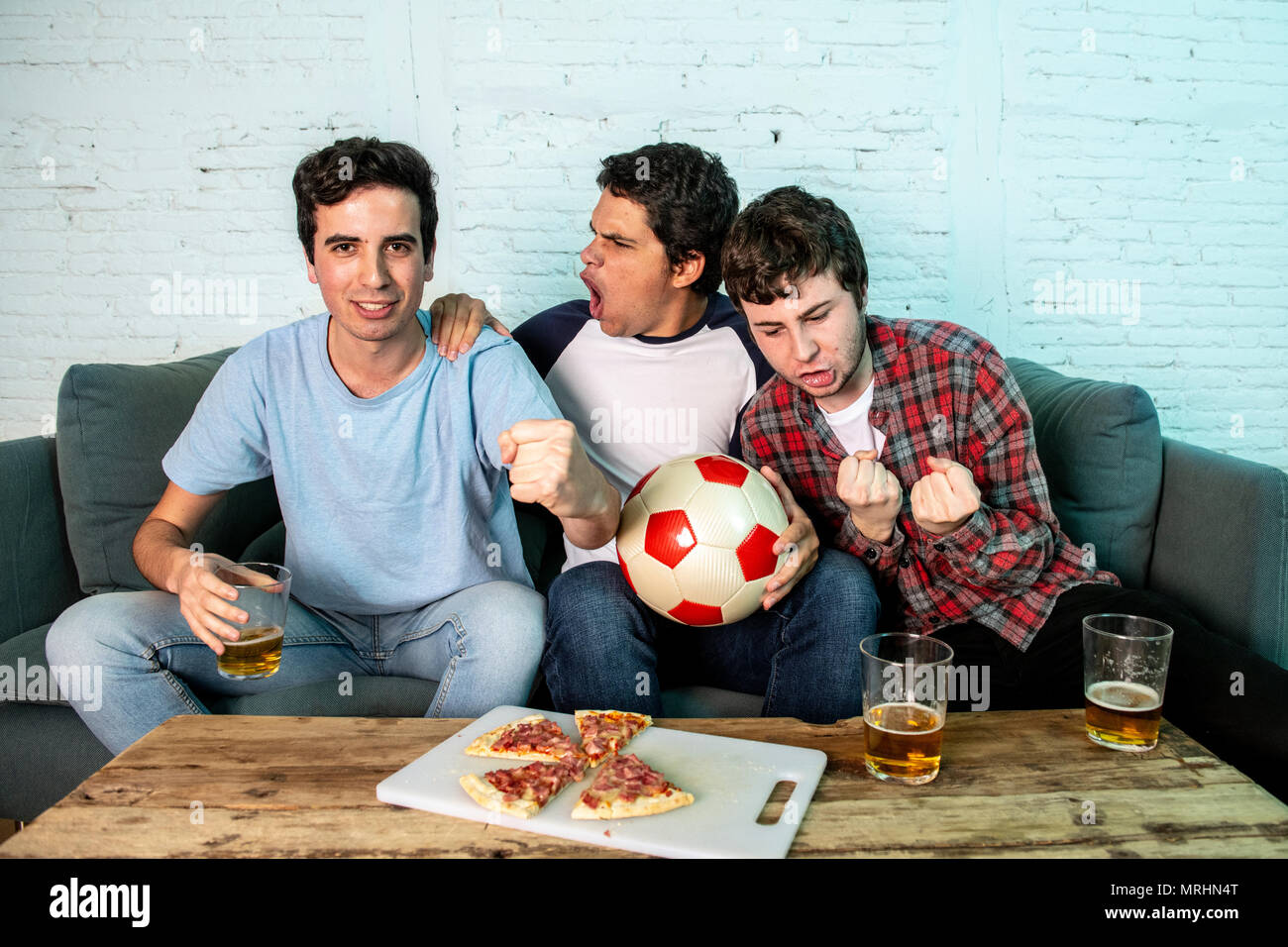 a happy and excited young group of football fans sitting on the sofa ...